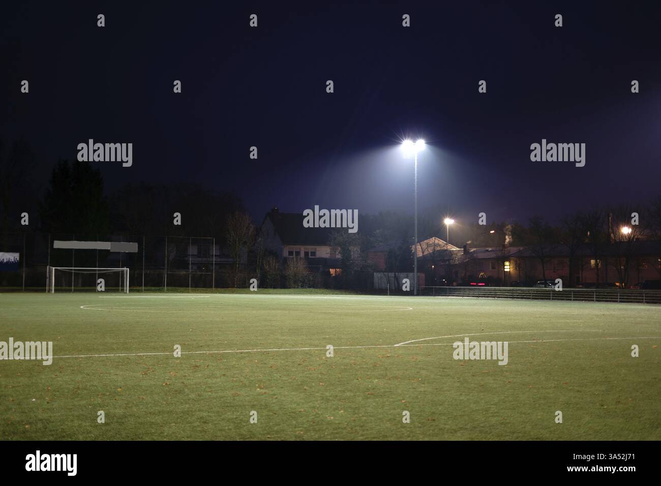 The green turf of a football pitch at night is illuminated by ...
