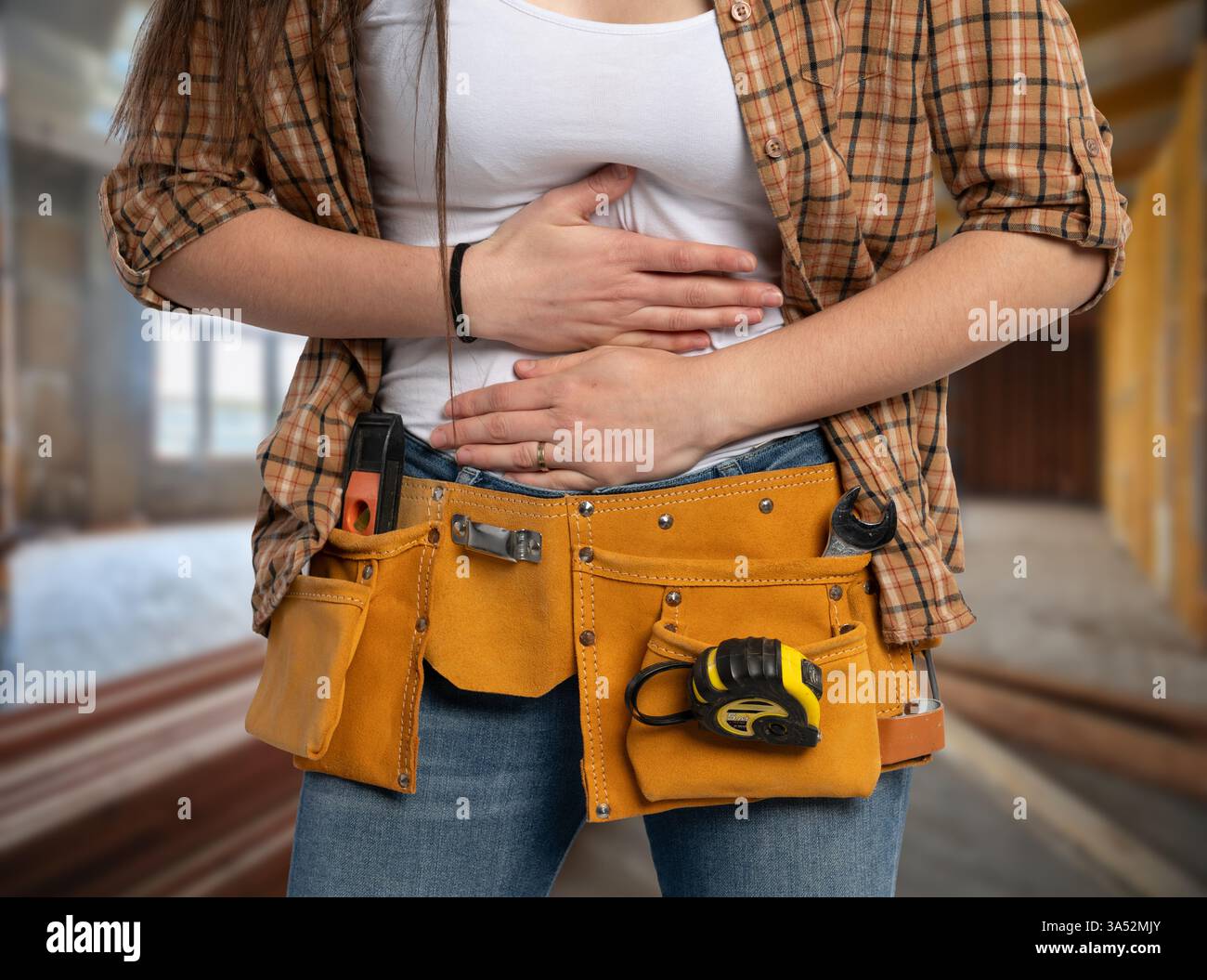 A close-up of a female construction worker holding her stomach in pain ...