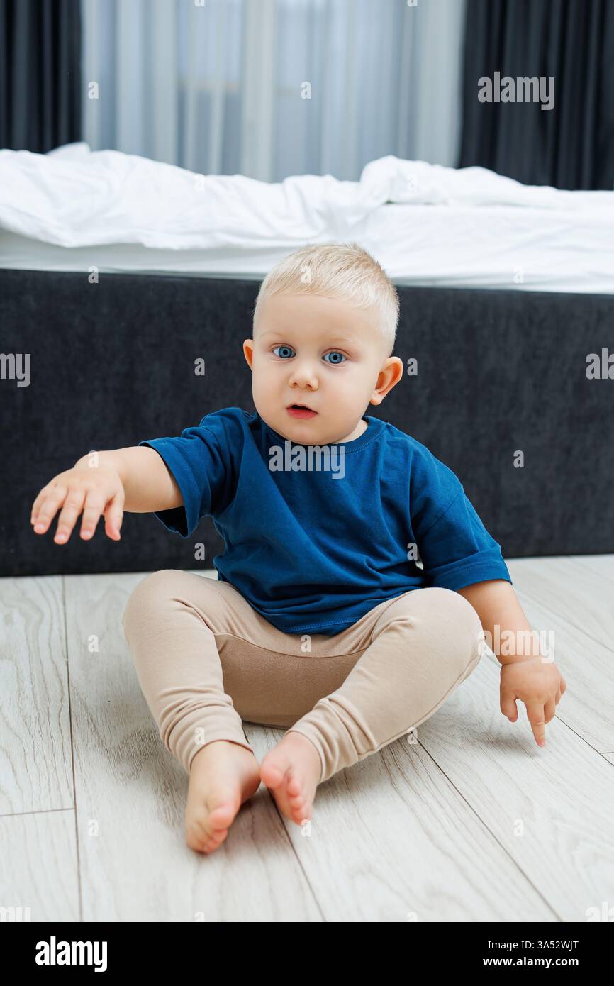 A joyful toddler sits on the floor, reaching out with curiosity ...