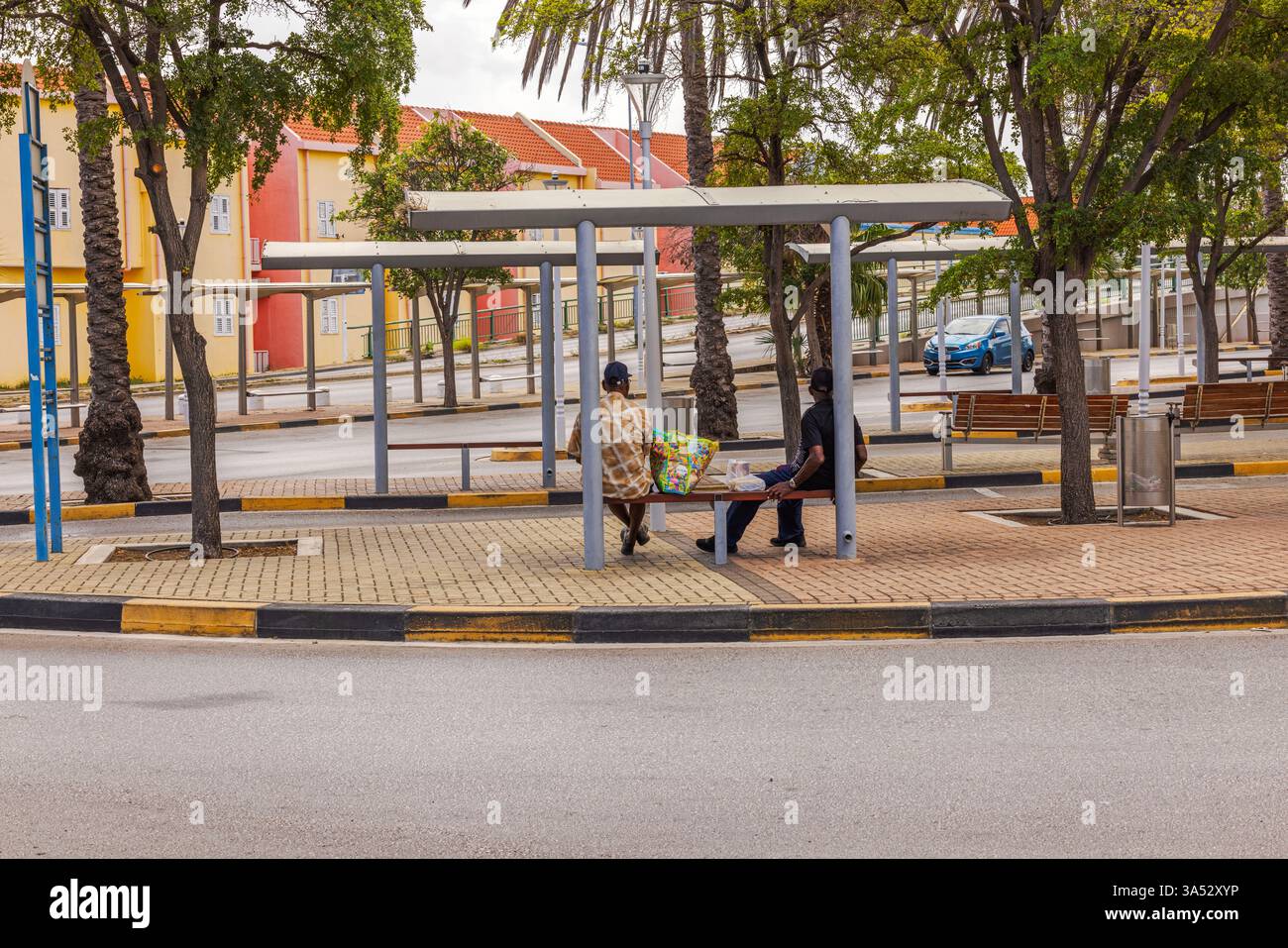 Two people sitting at bus stop with metal shelters, benches, trees, and ...