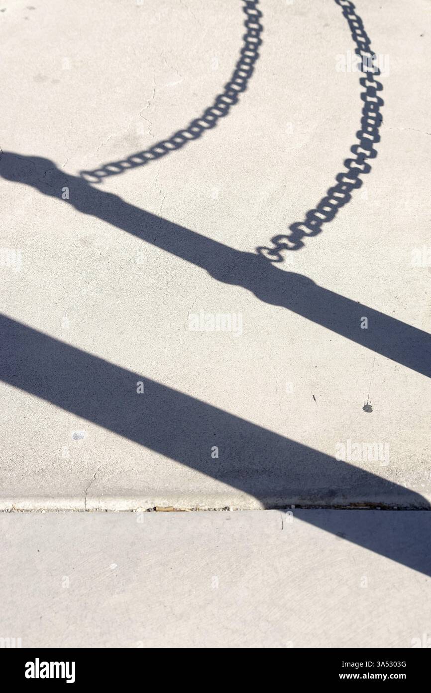 The silhouette of the shadow of a railing with chains on the asphalt of ...