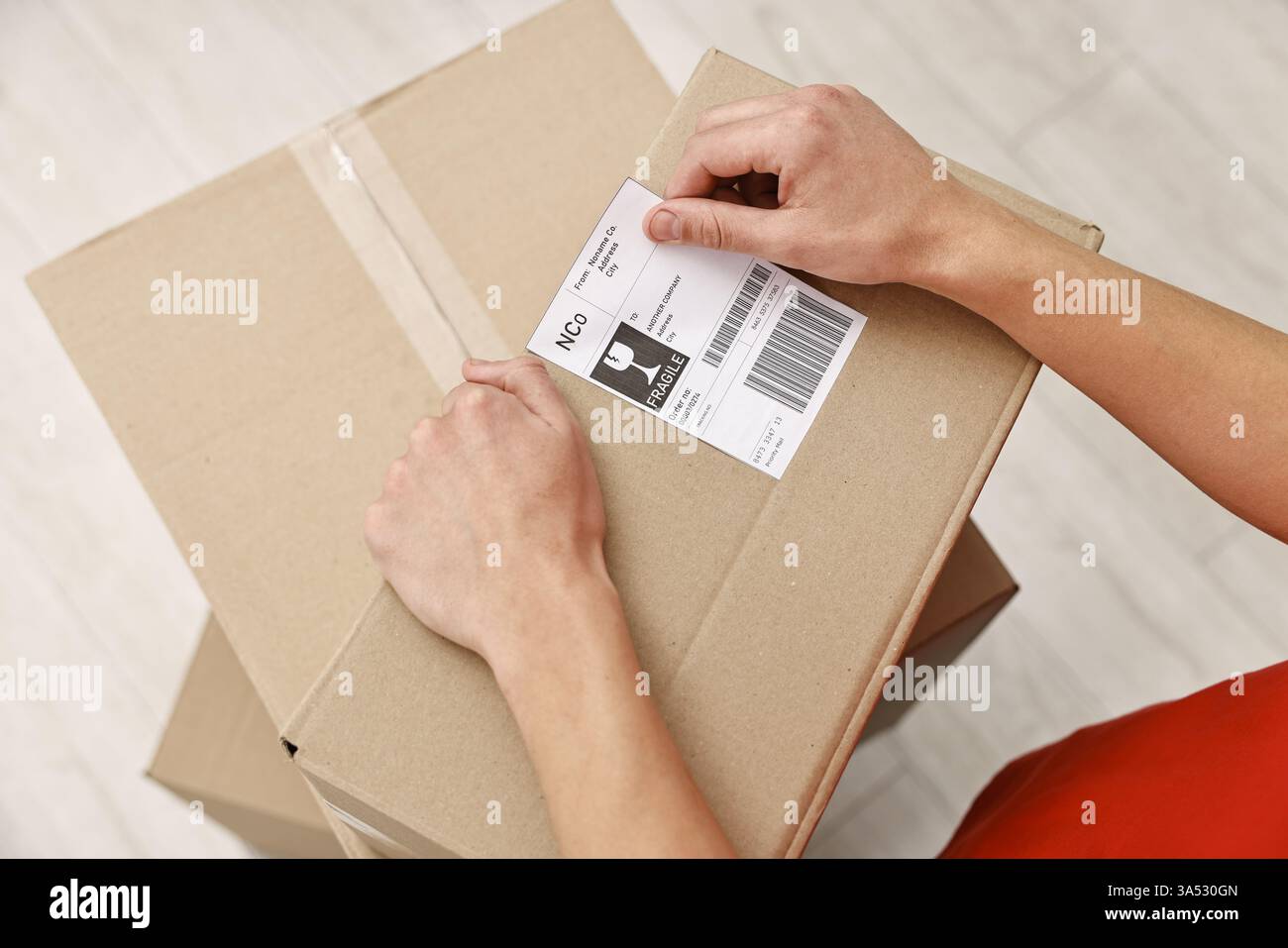 Man sticking shipping label with barcode on parcel indoors, above view ...