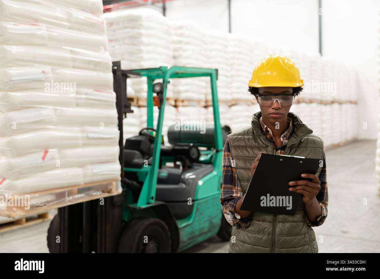 Warehouse worker wearing safety gear checking inventory with clipboard ...