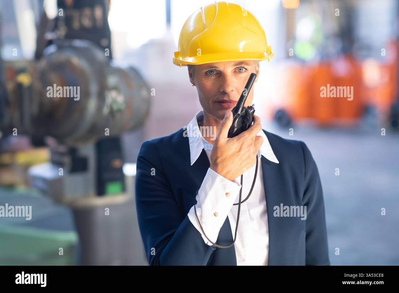 Woman in hard hat using walkie-talkie, managing operations in warehouse ...