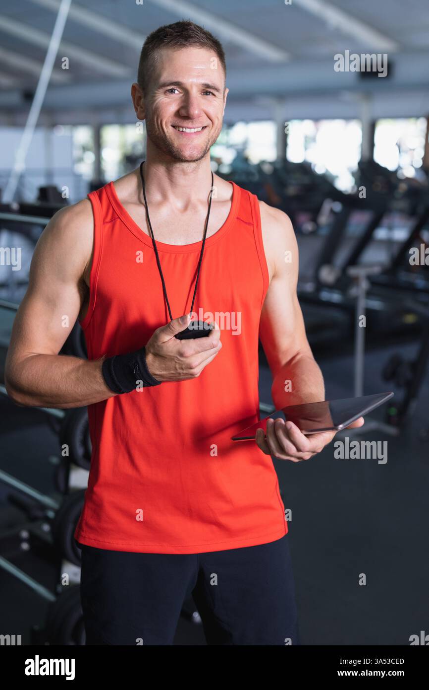 Fitness coach in gym holding stopwatch and tablet, smiling confidently ...