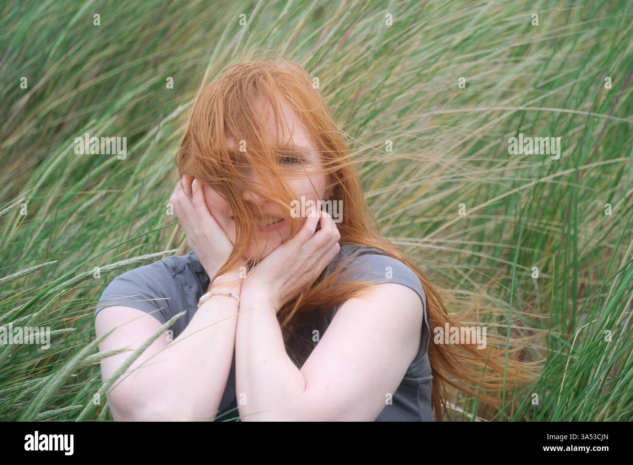 Vibrant redhead woman in tall beach grass, wind playfully tangling her ...
