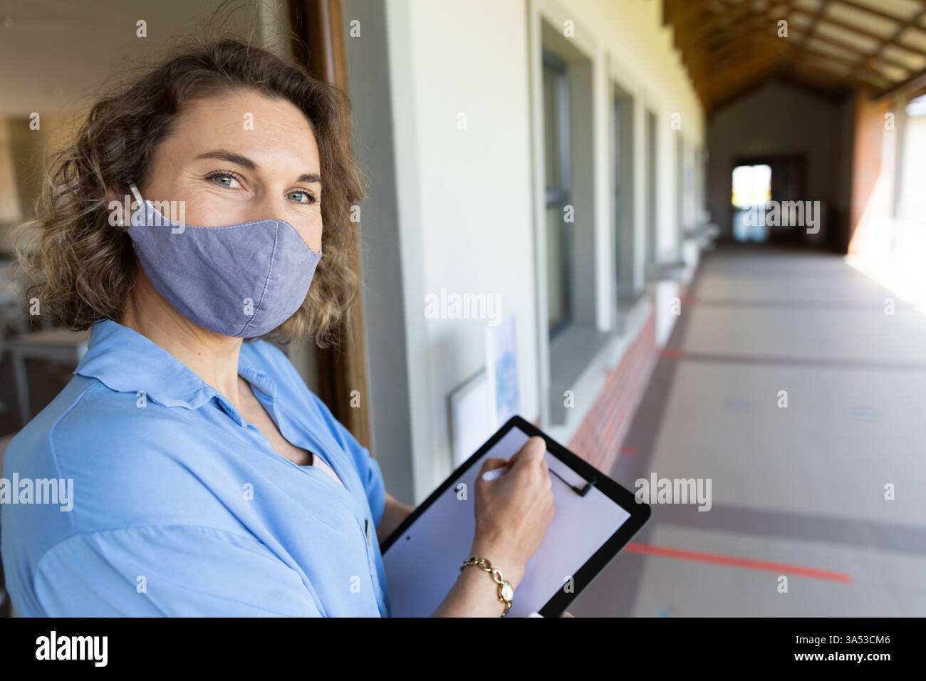 Teacher wearing mask holding clipboard, preparing for class in school ...