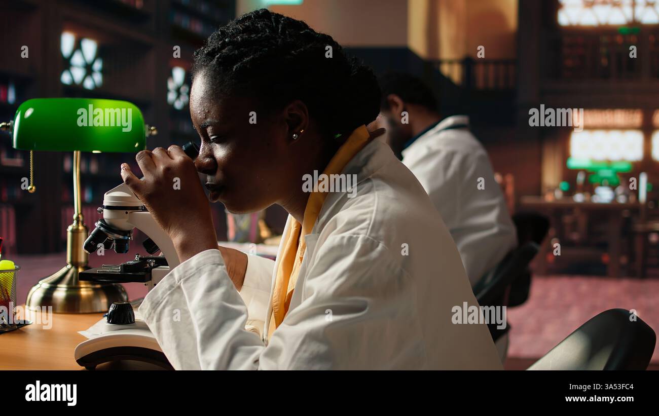 Black university student examining cells and organisms under microscope lenses, researching and ...