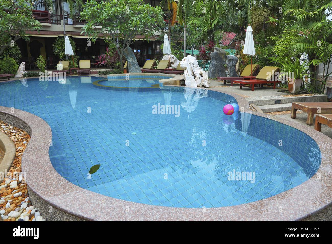 Two inflatable balls in pool with the transparent water, surrounded with palm trees, statues and ...