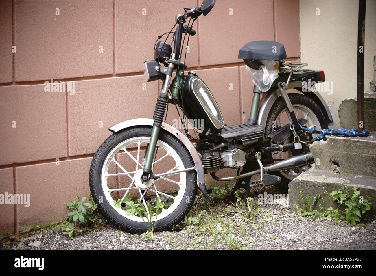 The side profile of an old vintage moped chained to a stair pillar ...