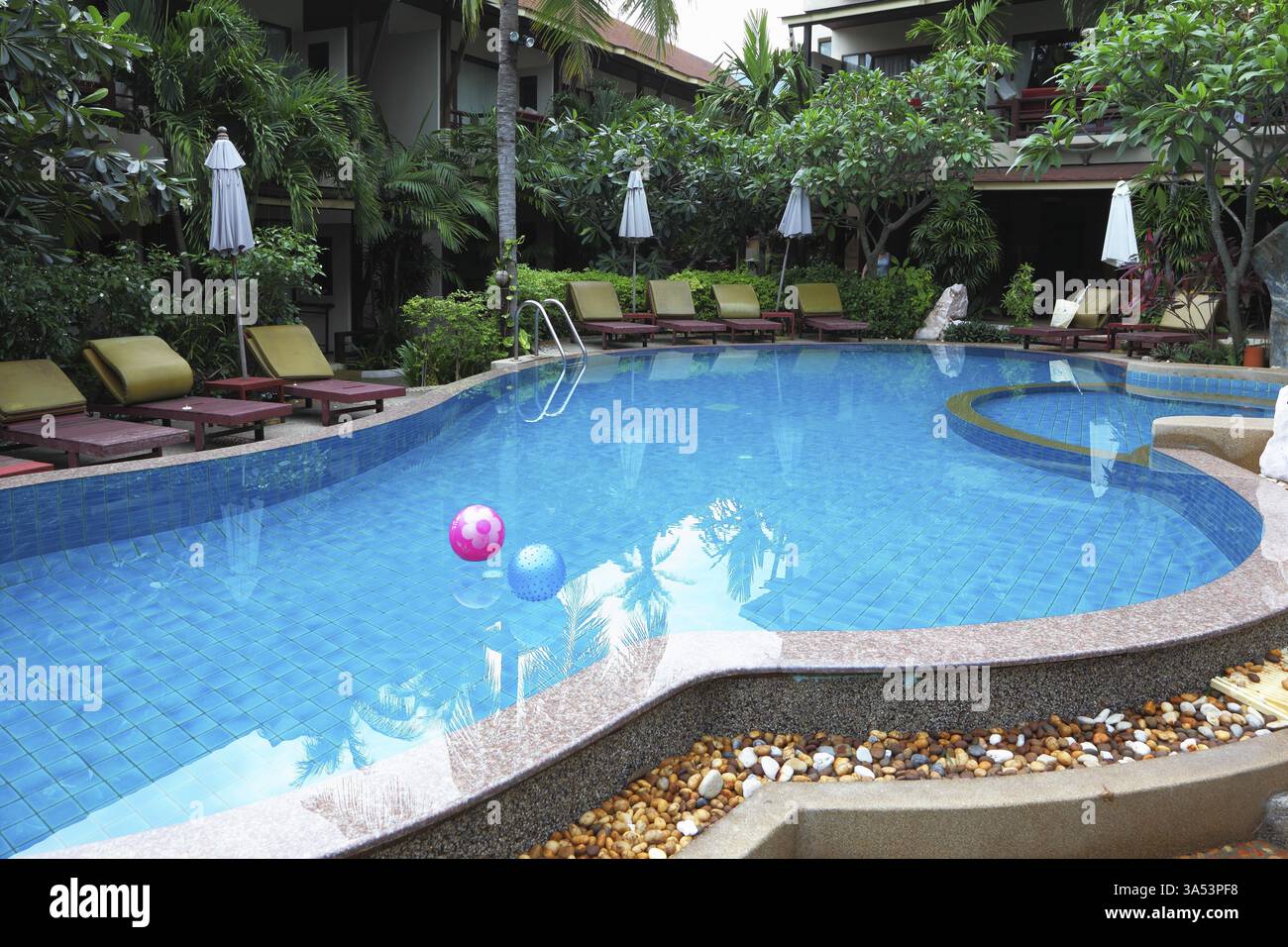Two inflatable balls -red and blue - in pool with the transparent water, surrounded with palm ...