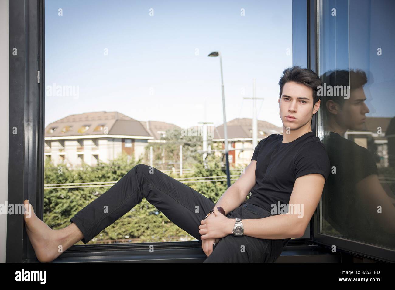Handsome young man sitting on open window sill looking at camera Stock ...