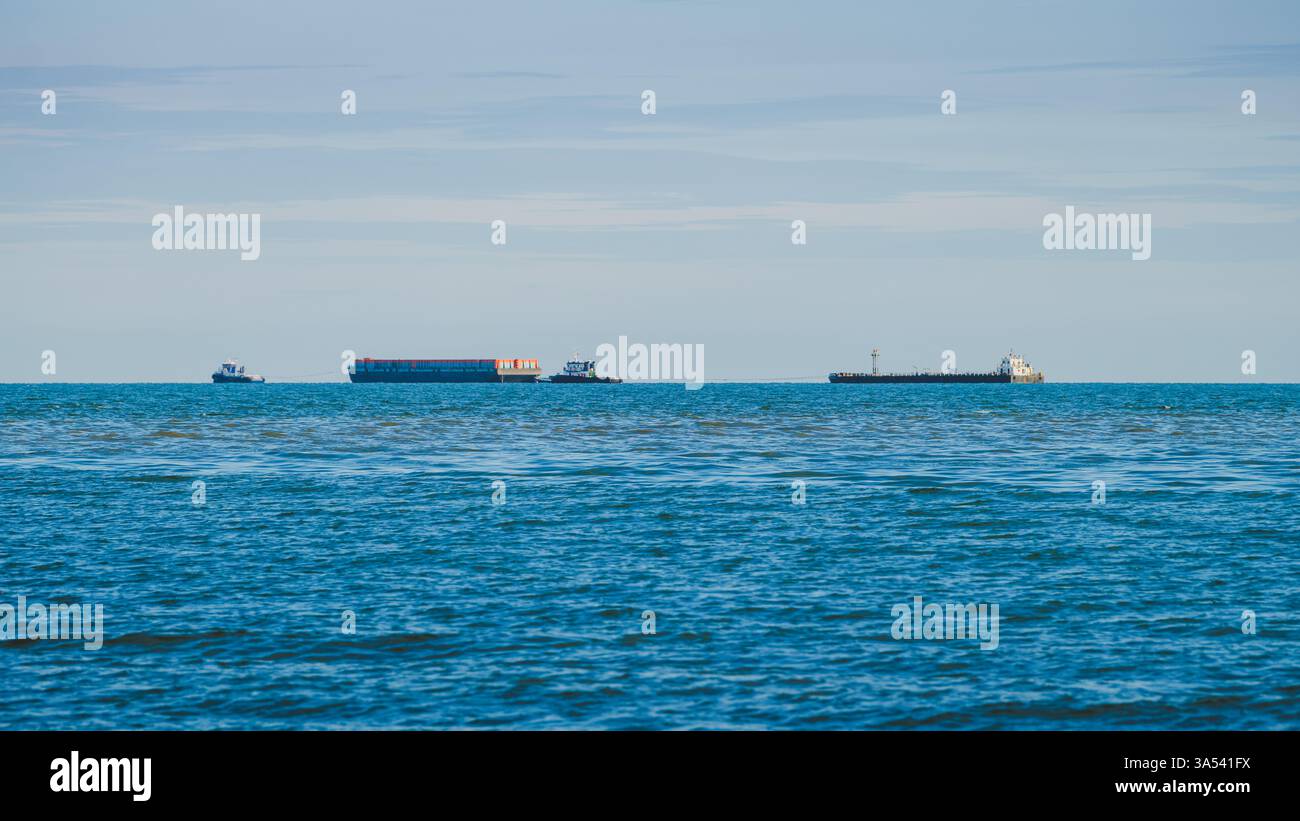 three vessels on the ocean, a central barge being towed by two tugboats ...