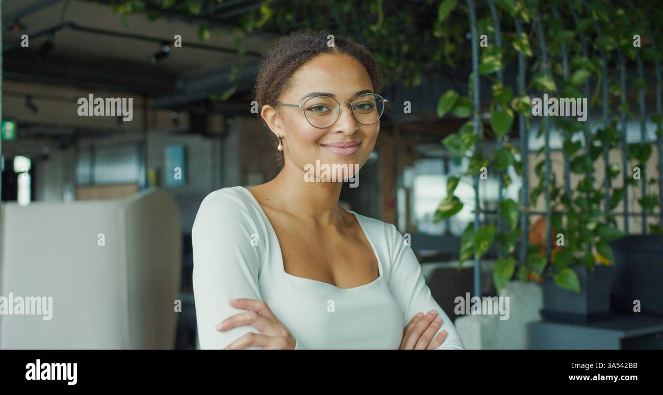 A confident, smiling young professional woman with glasses and arms ...