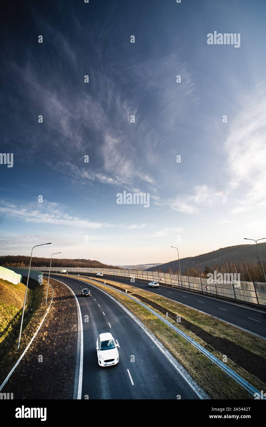 Cars traverse a winding highway surrounded by open fields and an ...
