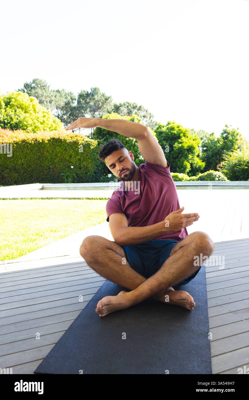 Man practicing yoga on mat outdoors, stretching arms and focusing on ...