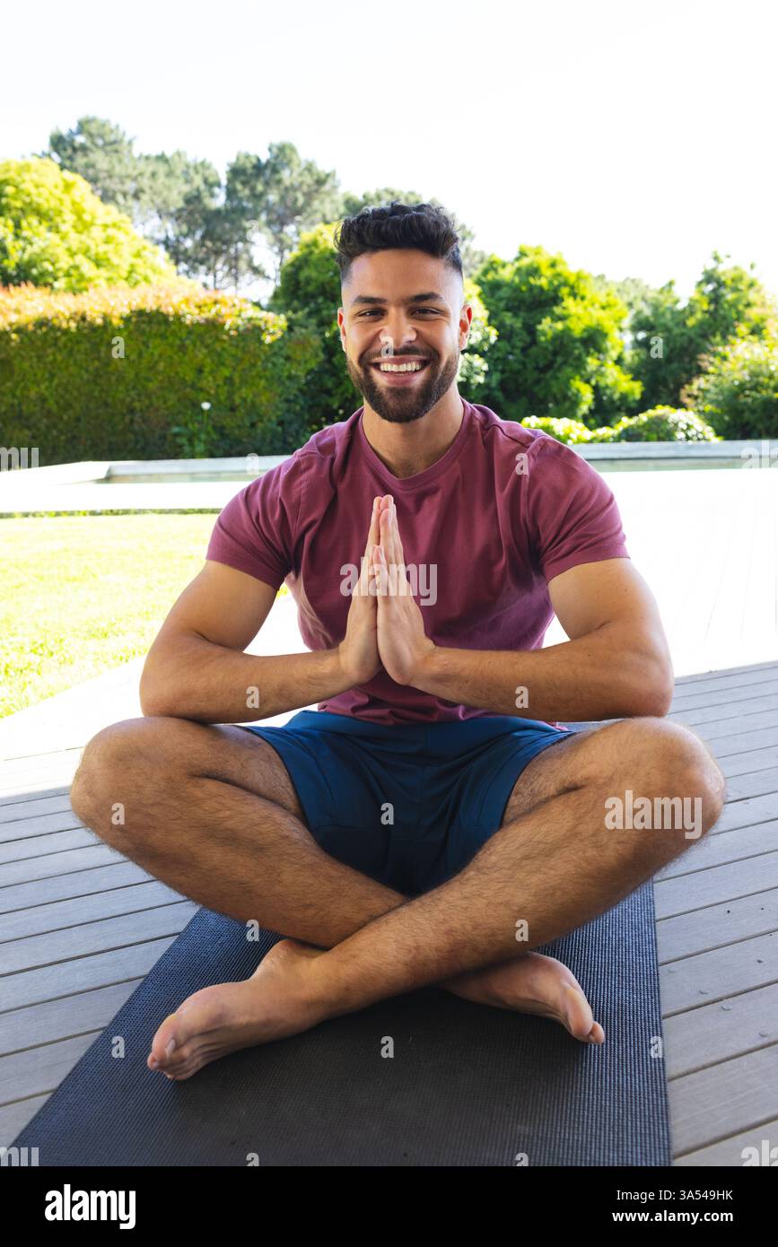 Smiling man sitting cross-legged on yoga mat outdoors, enjoying ...