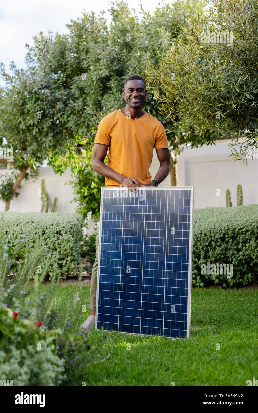 Smiling man holding solar panel in garden, promoting sustainable energy ...