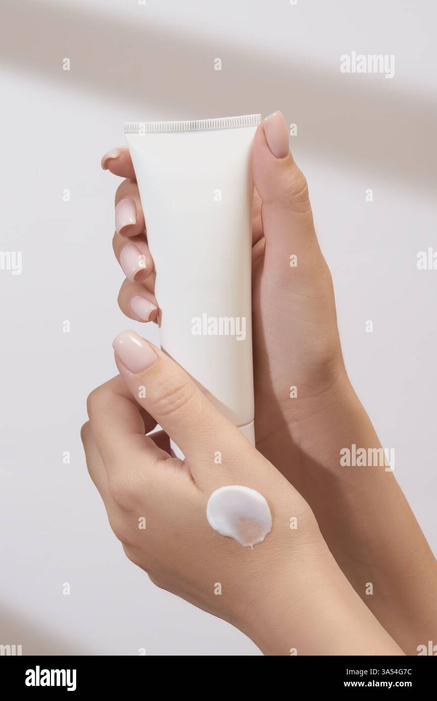 Woman's hand with applied hand cream and a mockup of white tube of ...