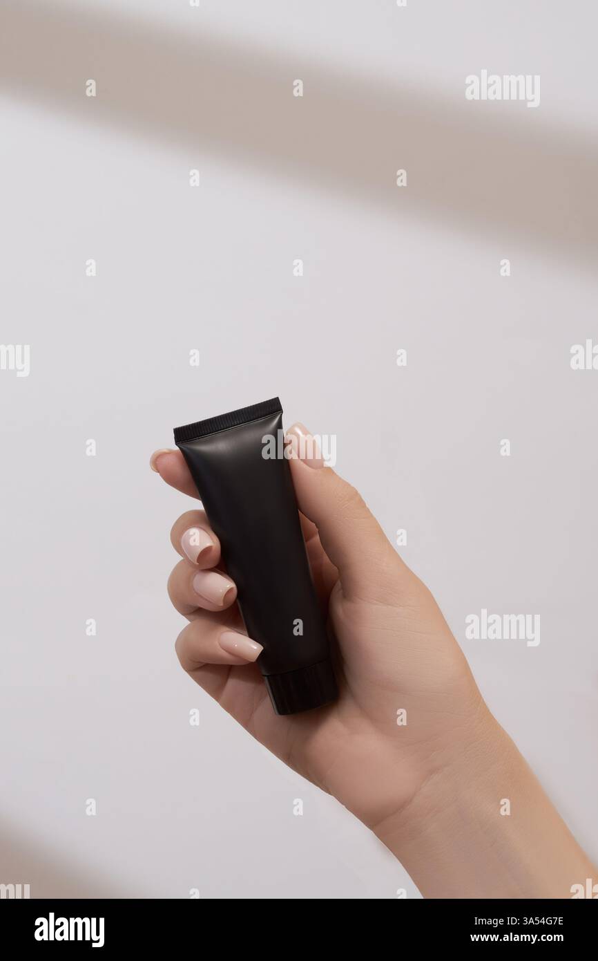 Woman's hand holds a mockup of black tube of cream. Unlabeled packaging ...