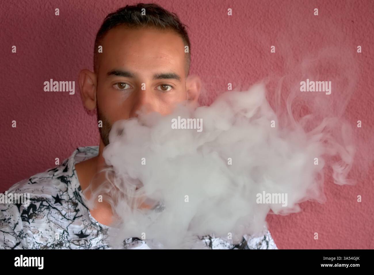 A young man sits in his bedroom, releasing a dense cloud of smoke into ...