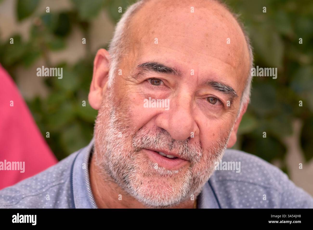 A close-up portrait of a mature bald man with a white stubble beard and ...