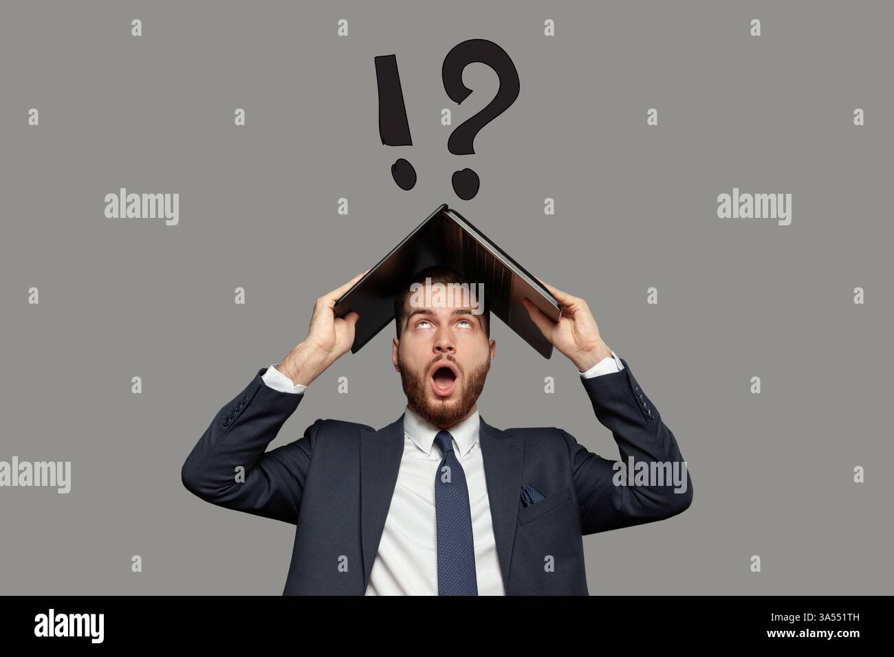 Emotional shocked businessman in suit with laptop on his head on grey ...