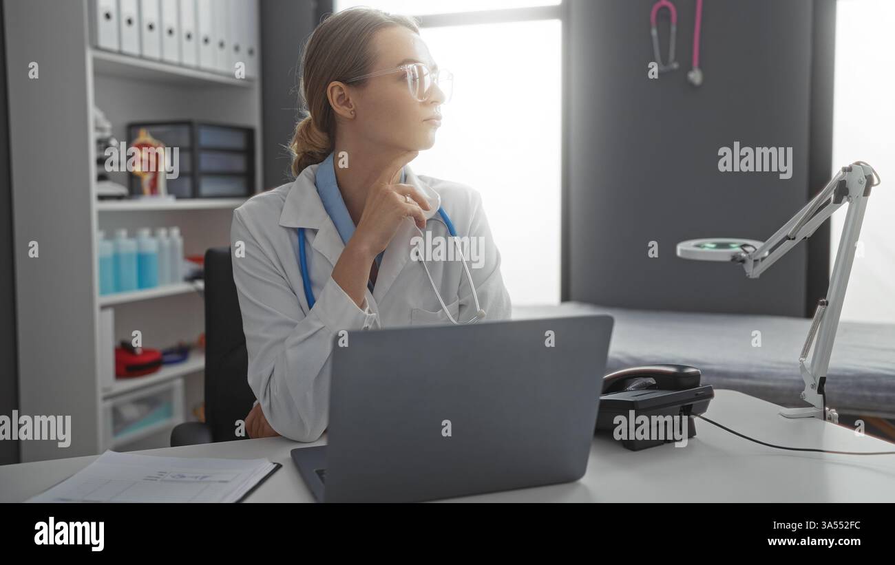 Woman in clinic looks thoughtful at desk with laptop and stethoscope ...