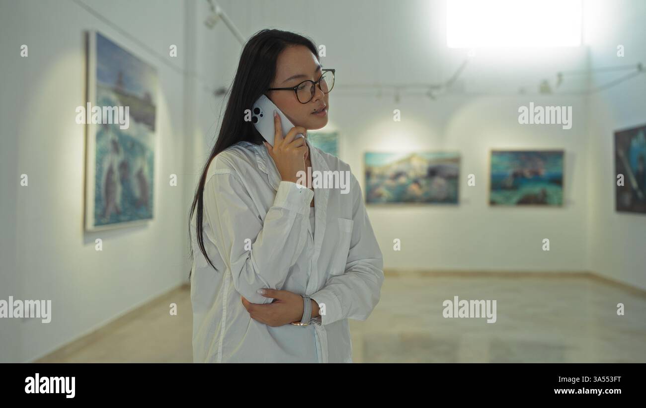 Woman talking on phone in art gallery, asian female admiring paintings, indoor museum setting ...