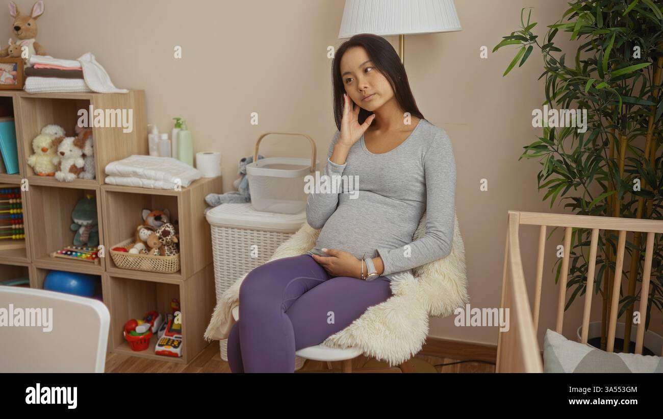 Pregnant asian woman sitting on a chair in a bedroom with a cradle and ...