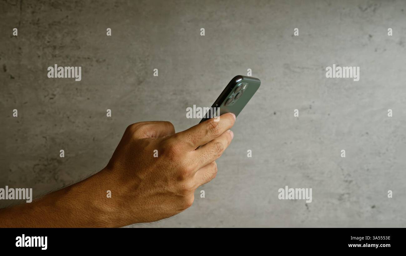 Man holding smartphone against concrete wall while texting Stock Photo ...