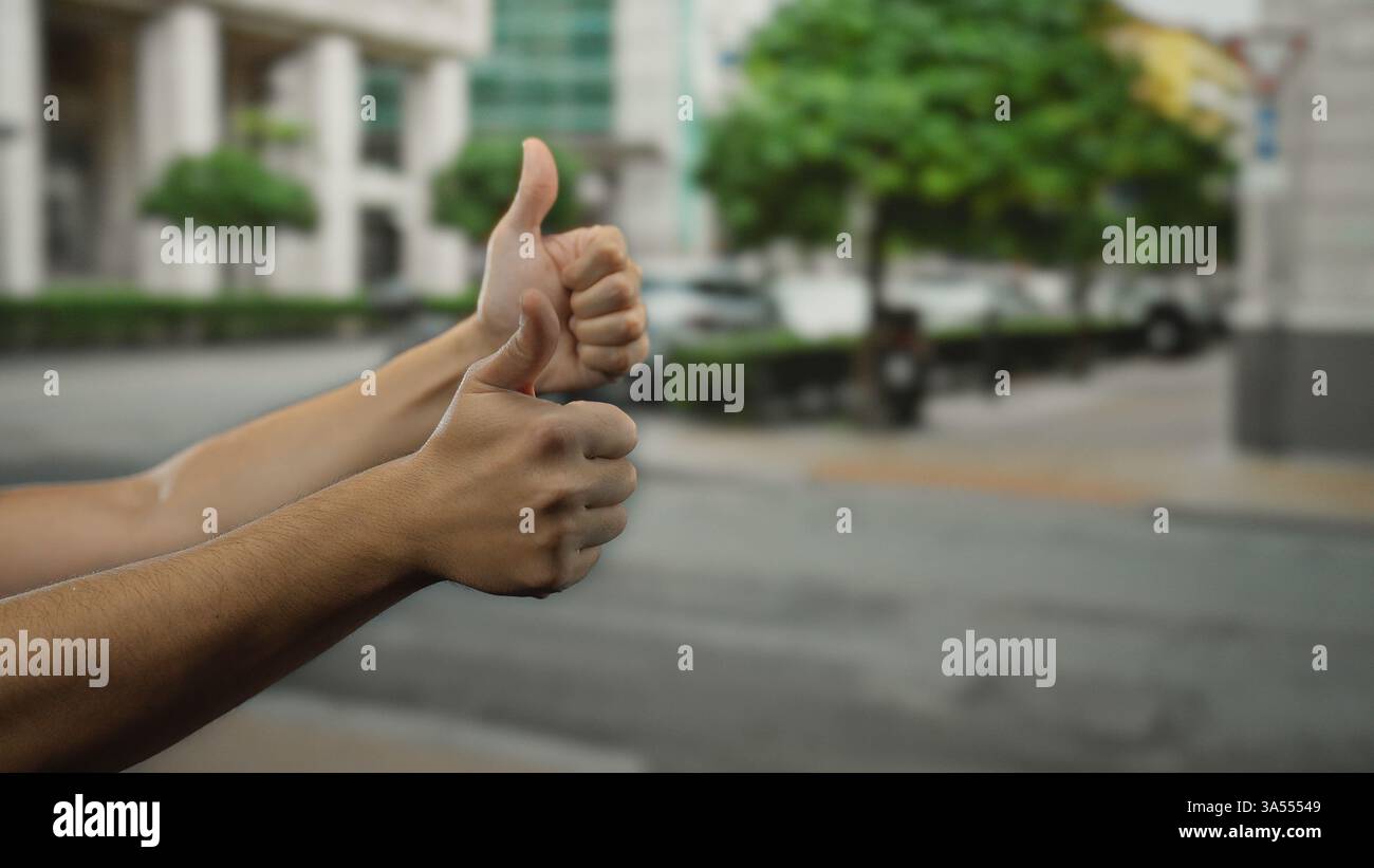 Two hands of a man giving a thumbs-up gesture on a busy city street ...