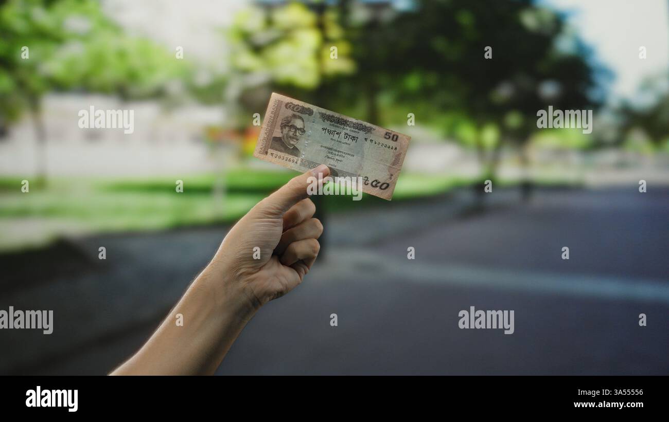 Hand holding bangladeshi taka outdoors on a city street, capturing a ...