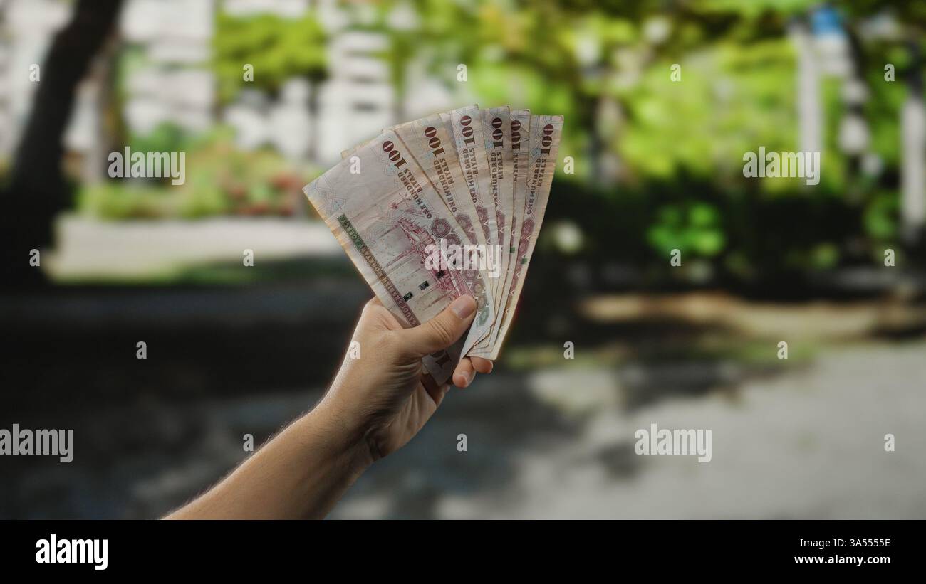 Man holding saudi arabian riyal banknotes in hand outdoors in a park ...