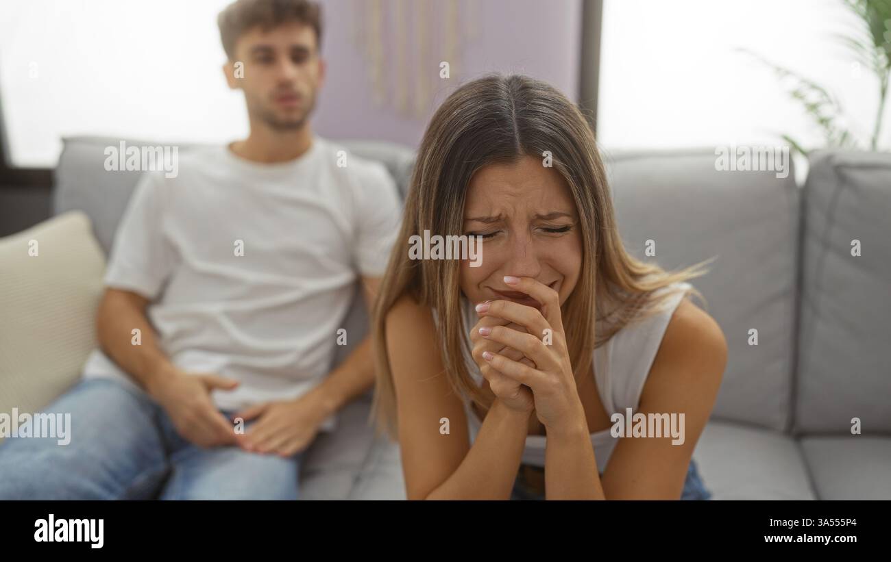 Woman crying on couch in living room with man in background, depicting ...