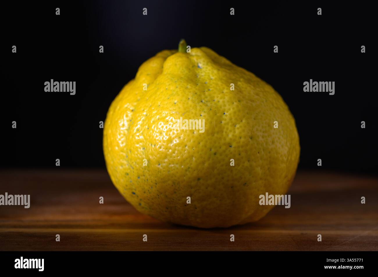A bright yellow citrus fruit on wood showcases its bumpy skin and ...