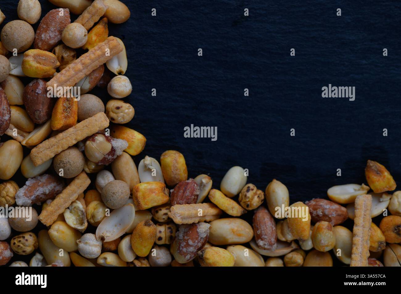 A diverse collection of snacks fills one corner of a dark surface ...