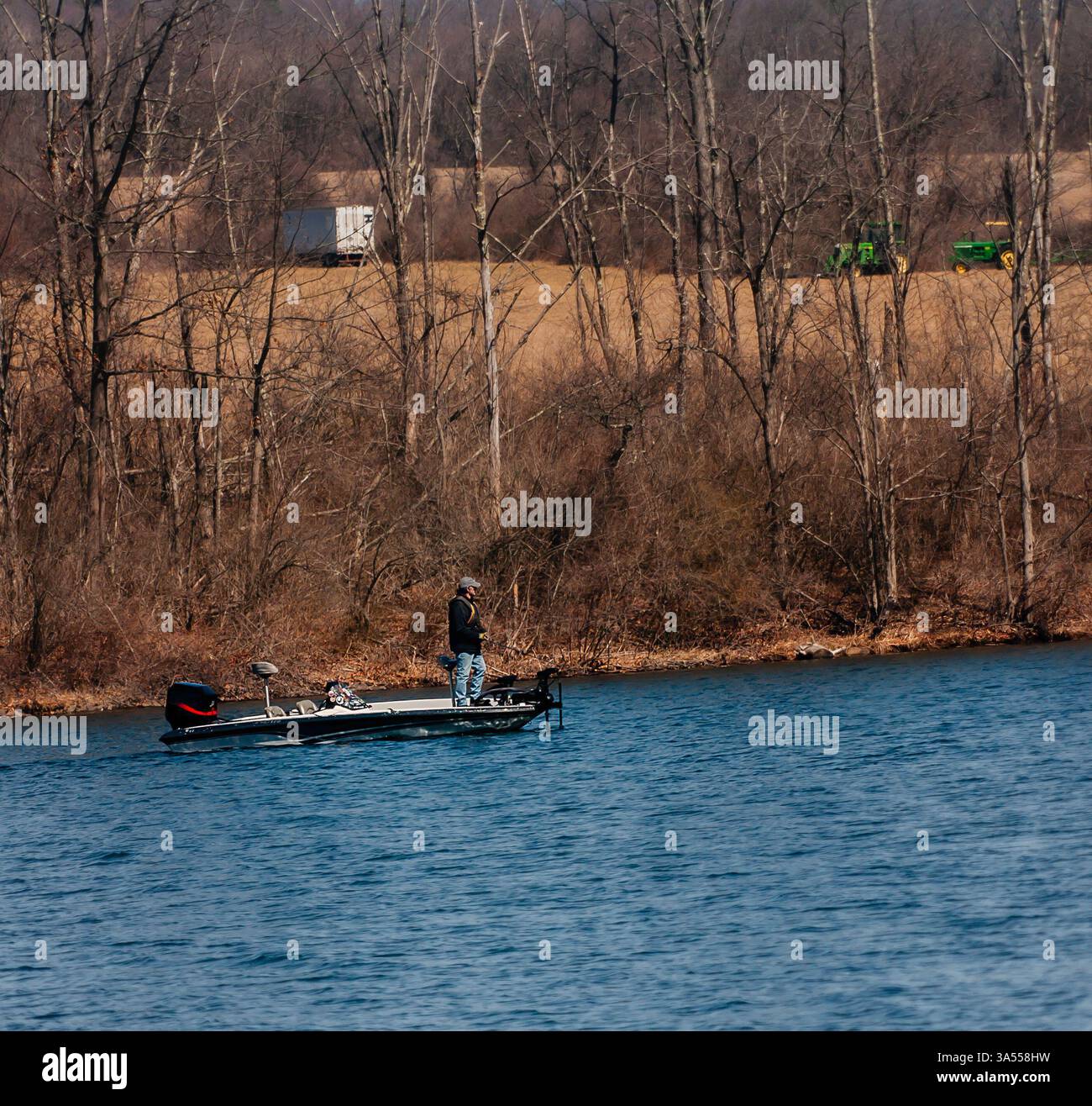 Man standing fishing from boat on a freshwater lake with fishing rod ...