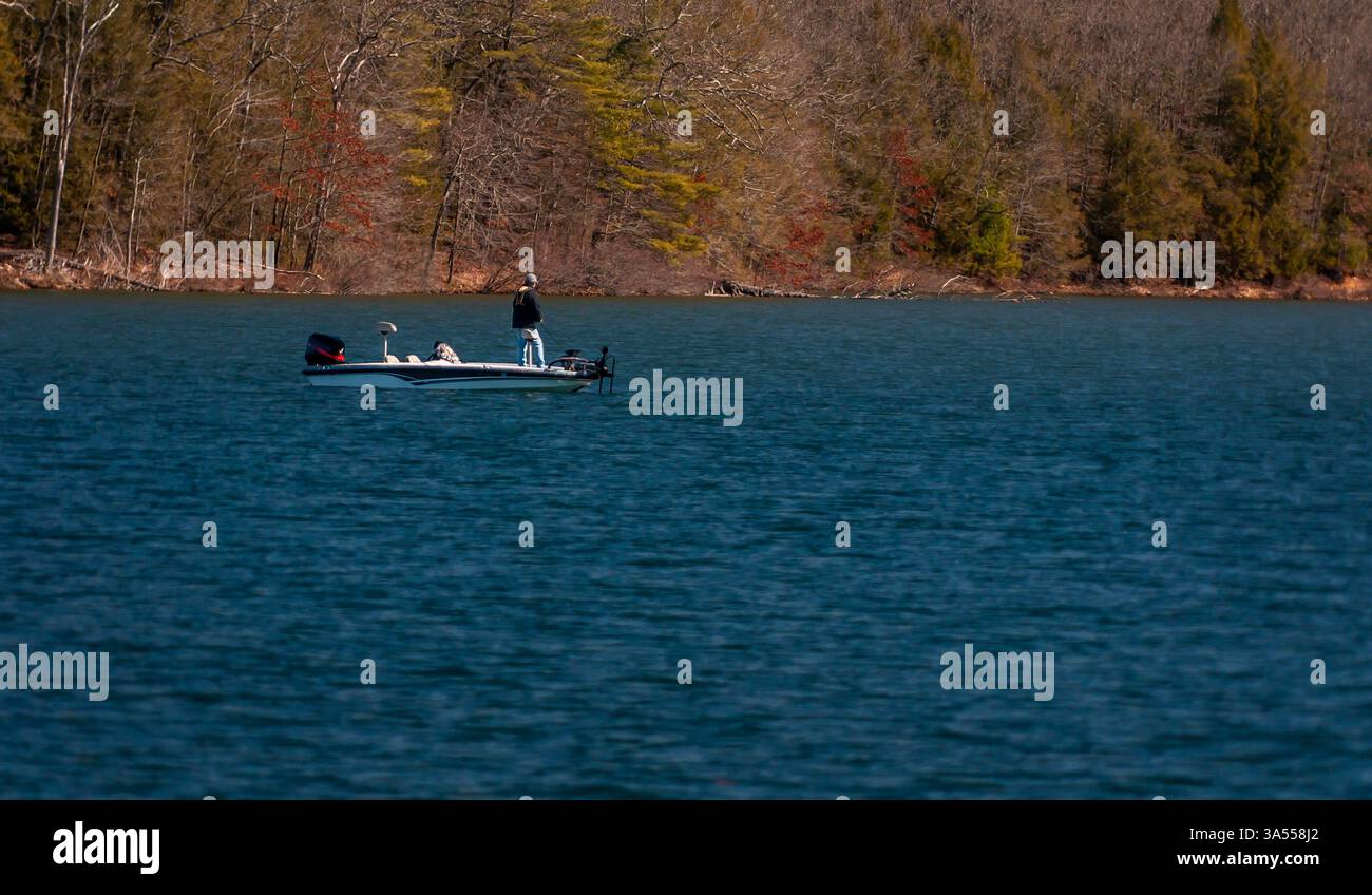 Man standing fishing from boat on a freshwater lake with fishing rod ...