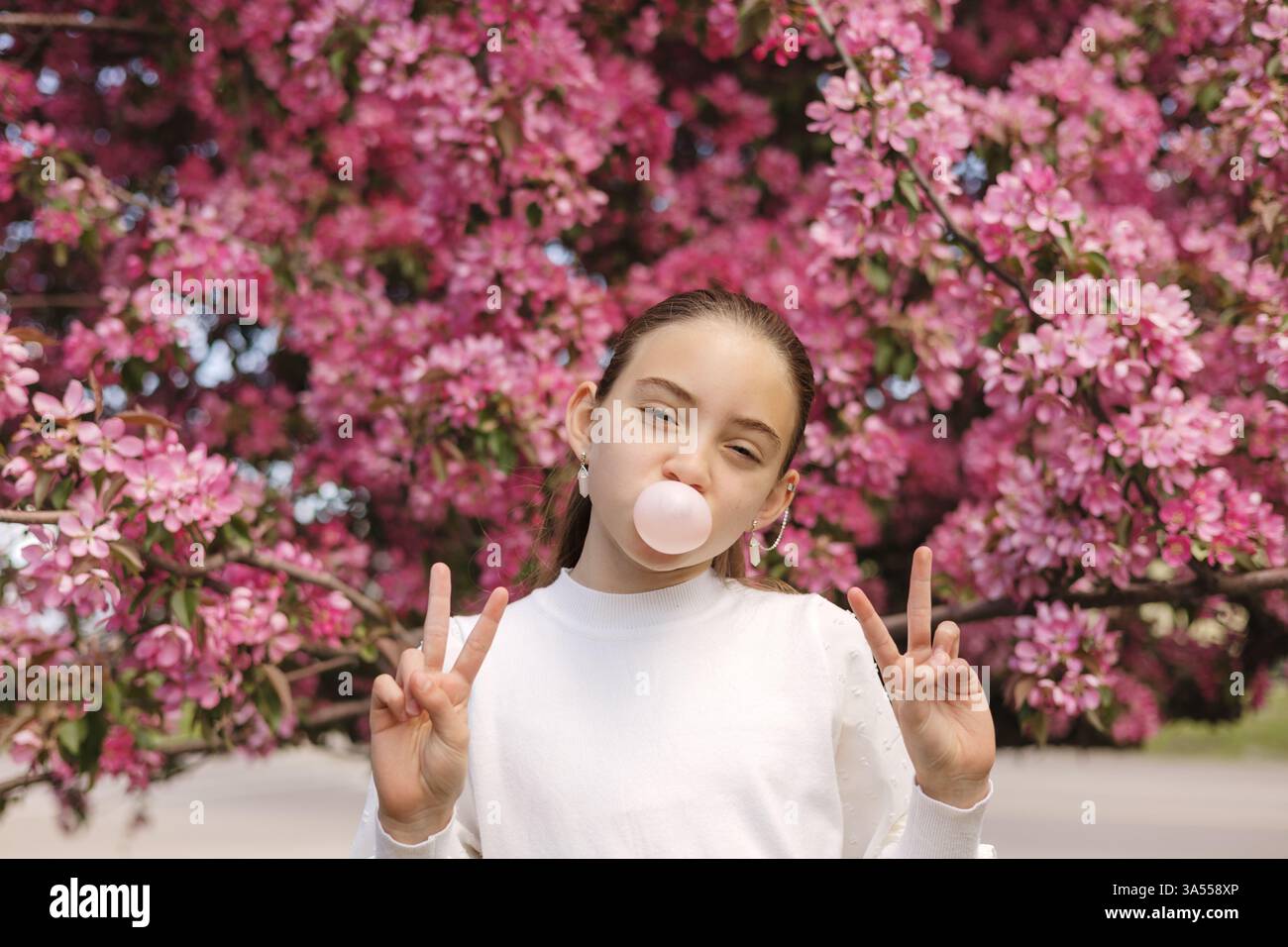 Adolescent girl making peace signs and blowing a pink bubble Stock ...