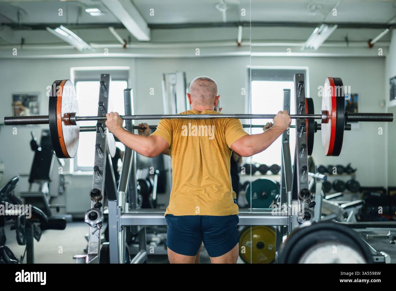 Muscular man lifting a barbell for squats in the gym Stock Photo - Alamy