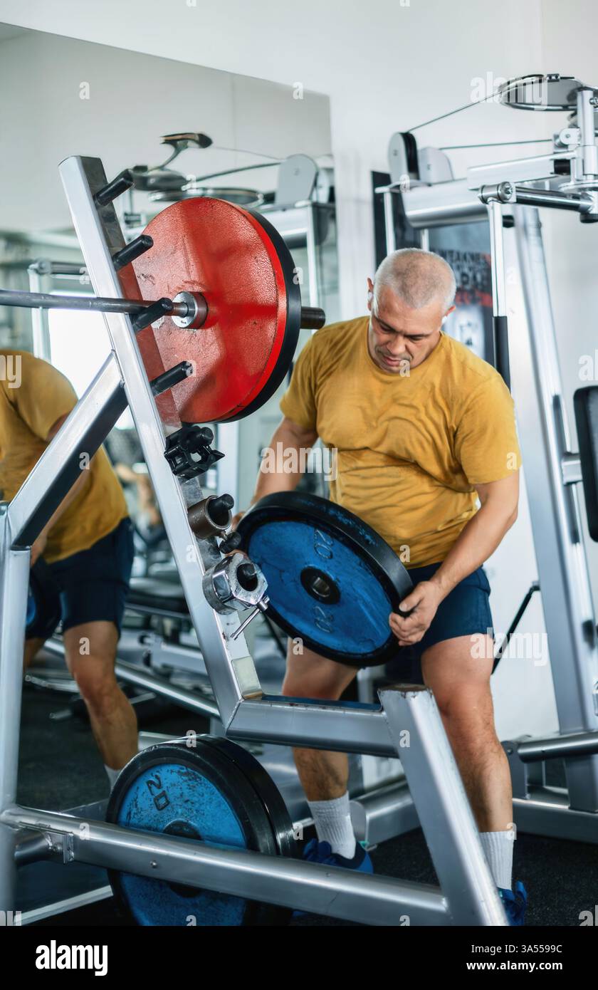 Muscular man adjusting weight plates on a squat machine in the gym ...