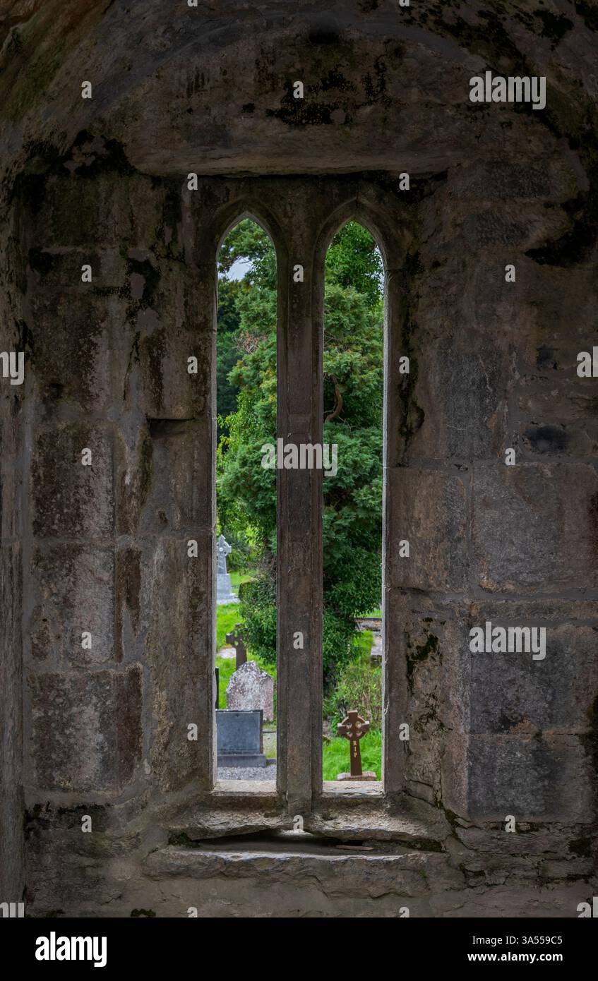 A view through a narrow, gothic-style arched window in Muckross Abbey ...