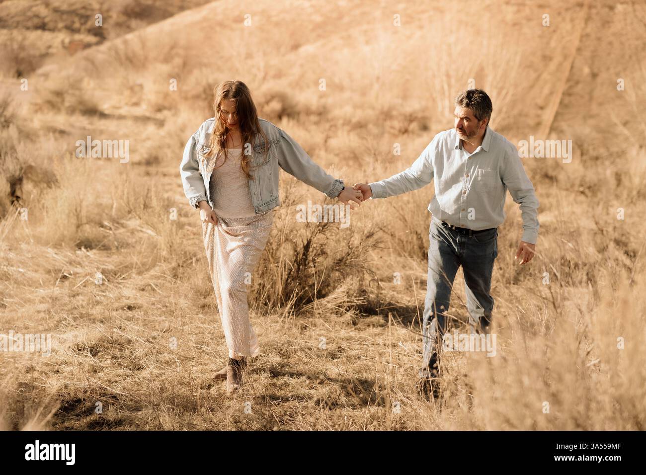 A couple walks hand in hand, exploring a grassy field in spring Stock ...