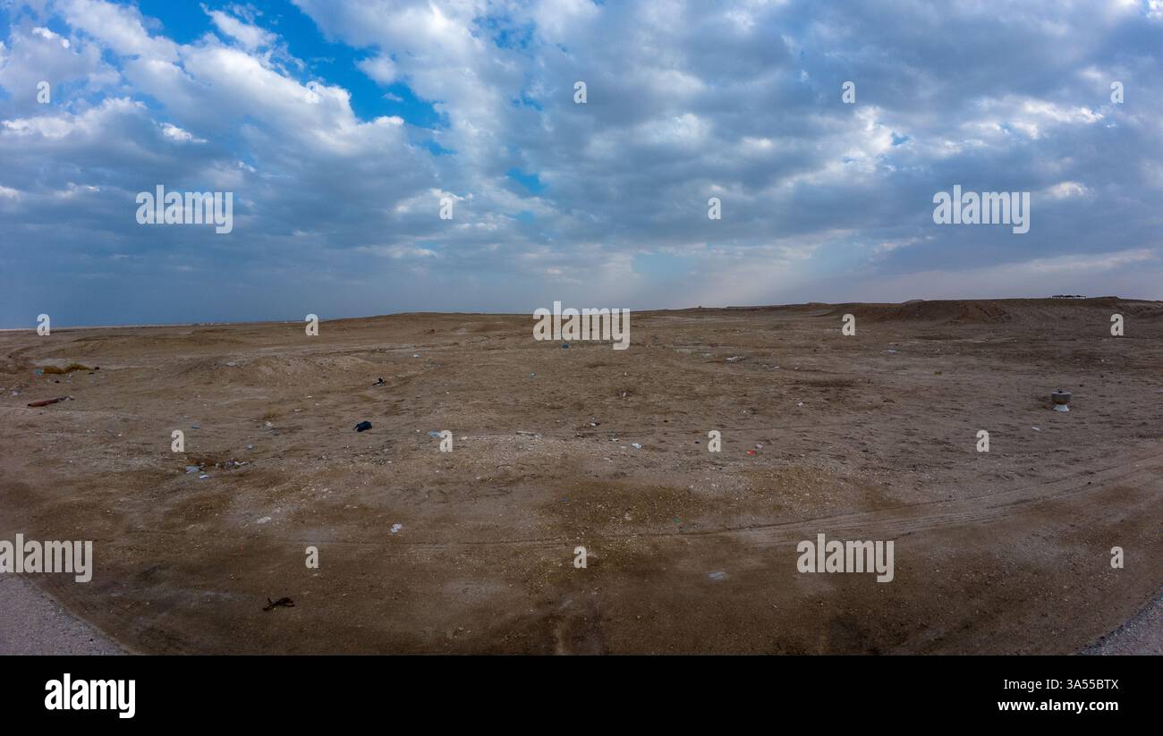A vast, barren desert landscape under a partly cloudy sky, with scattered debris on the ground ...