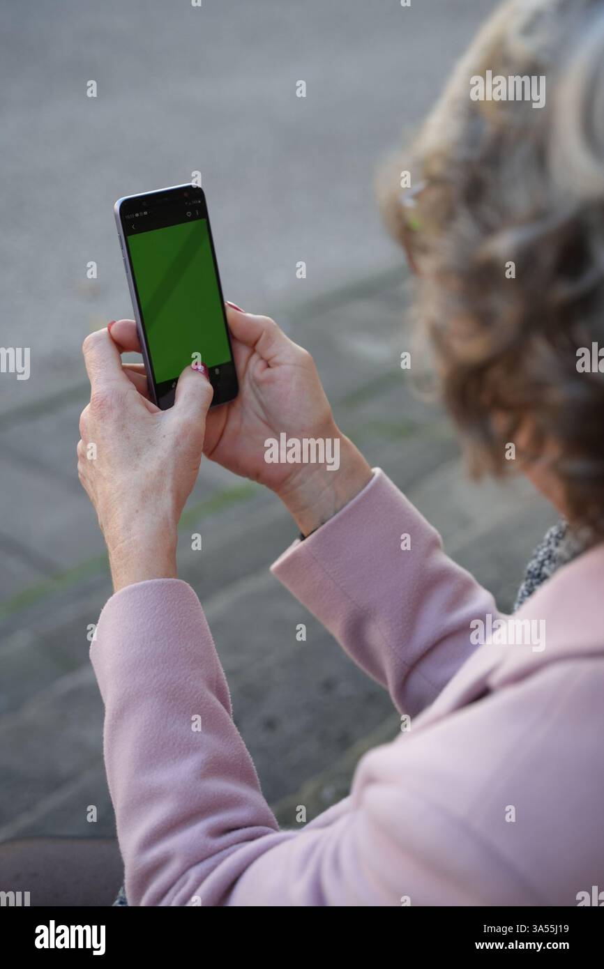 Woman in a pink coat using a smartphone with a green screen while ...