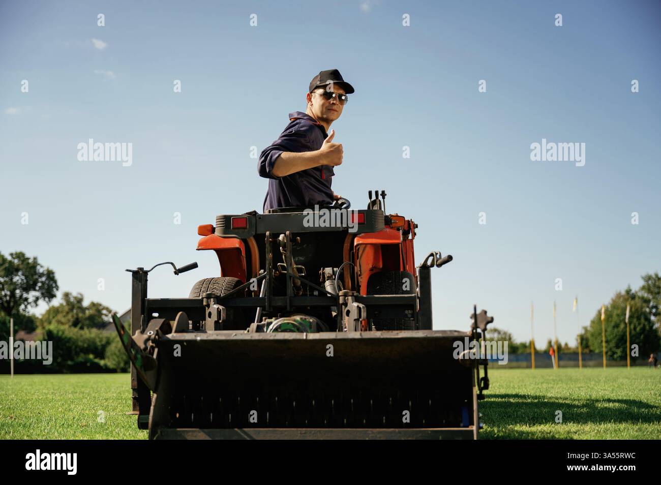 Driving, looks behind, shows thumb up. Man is with utility tractor with ...