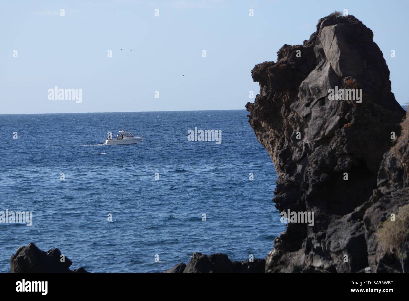 Volcanic cliffs on Tenerife’s coast with a boat sailing the Atlantic ...