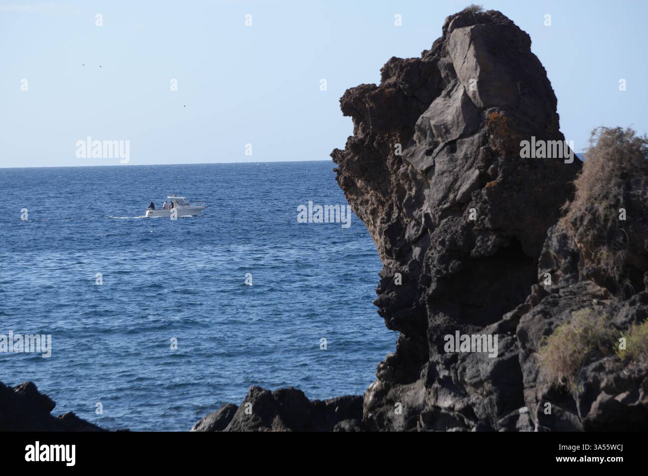 Volcanic cliffs on Tenerife’s coast with a boat sailing the Atlantic ...