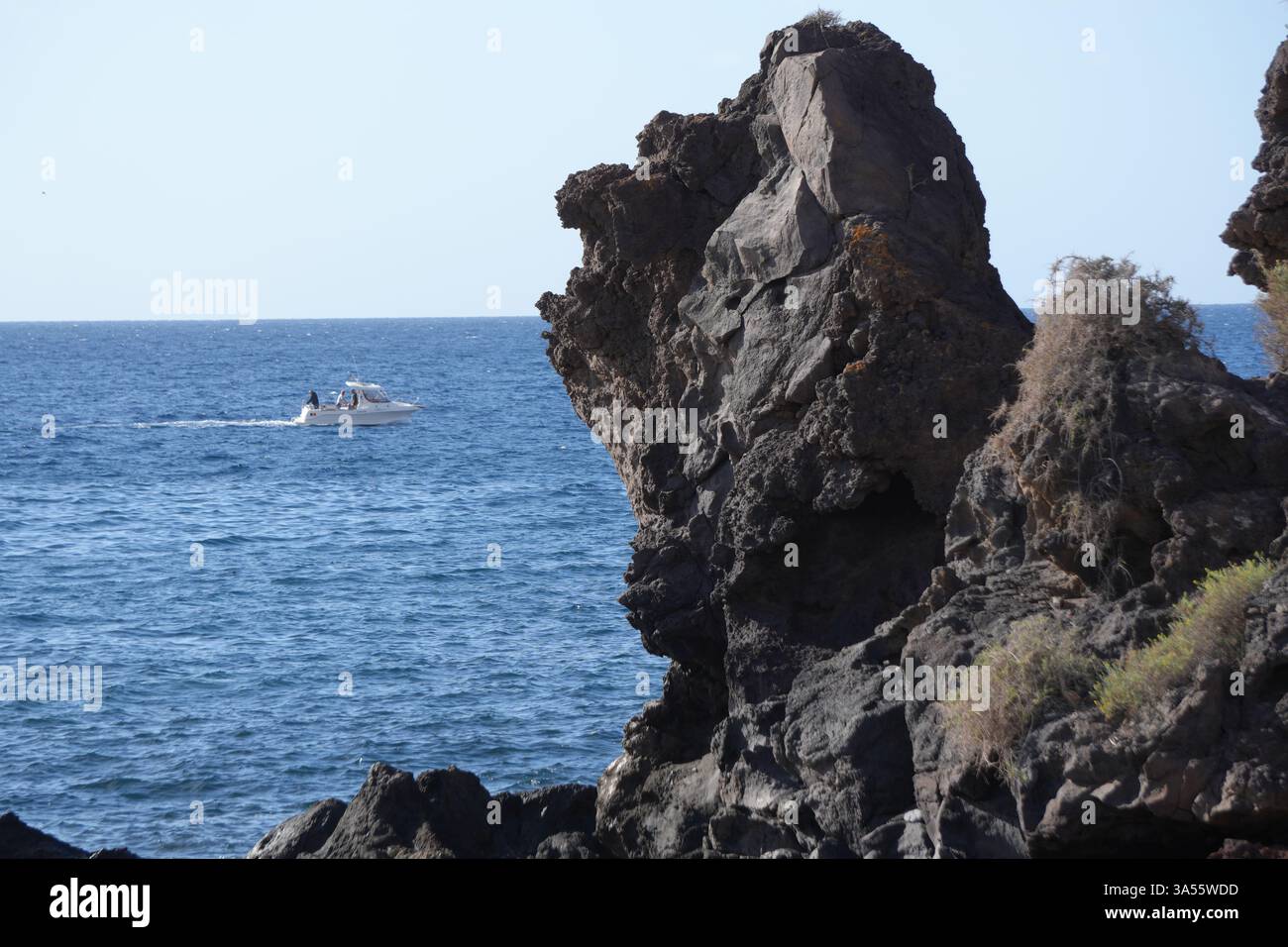 Volcanic cliffs on Tenerife’s coast with a boat sailing the Atlantic ...